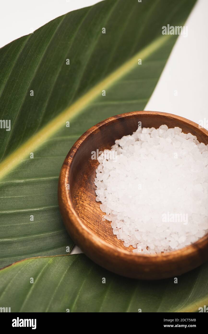 close up view of sea salt in wooden bowl, and green leaves on white ...