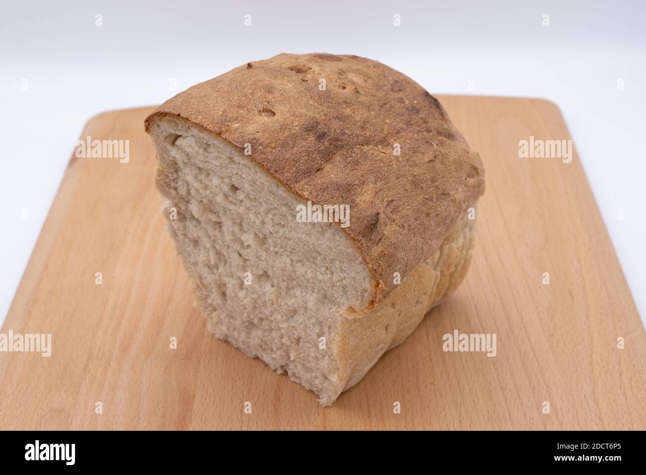 A plain white loaf cut in half on a bread board isolated against a ...