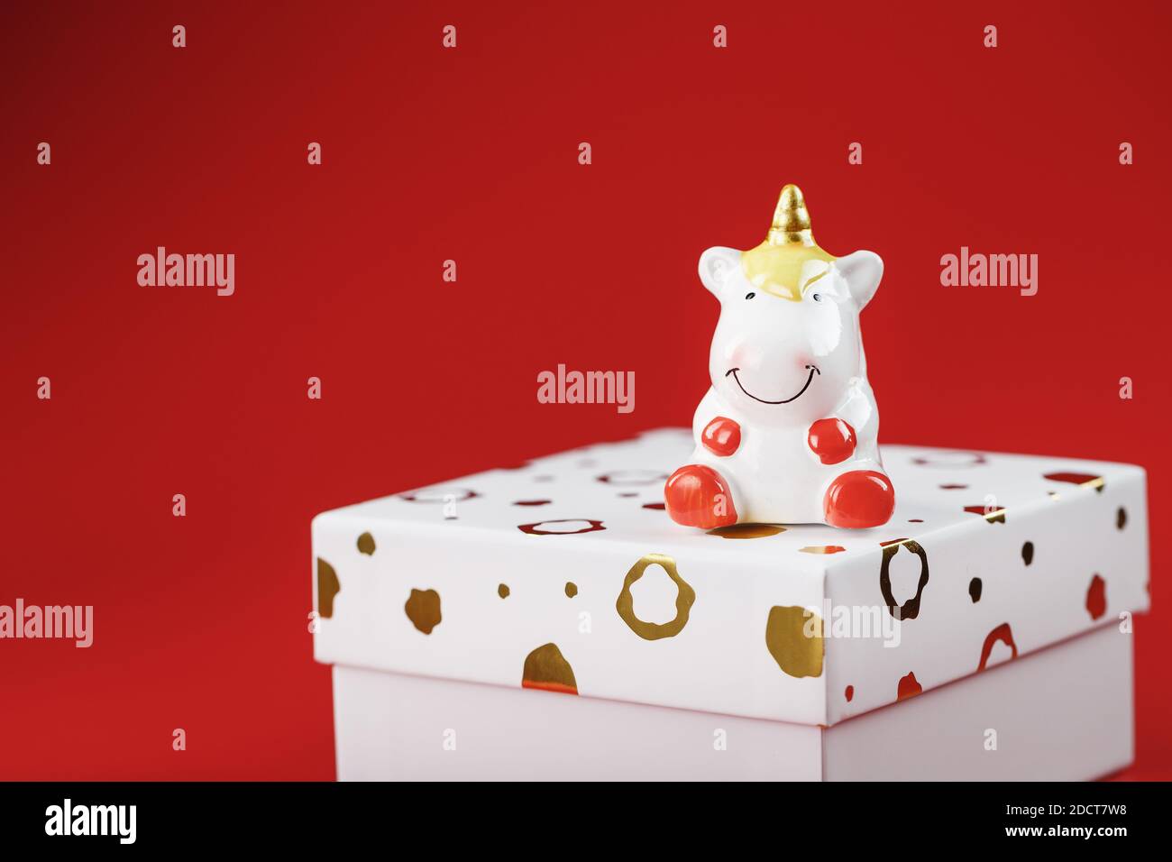 A little figure of a unicorn on the box with a gift on a red background ...