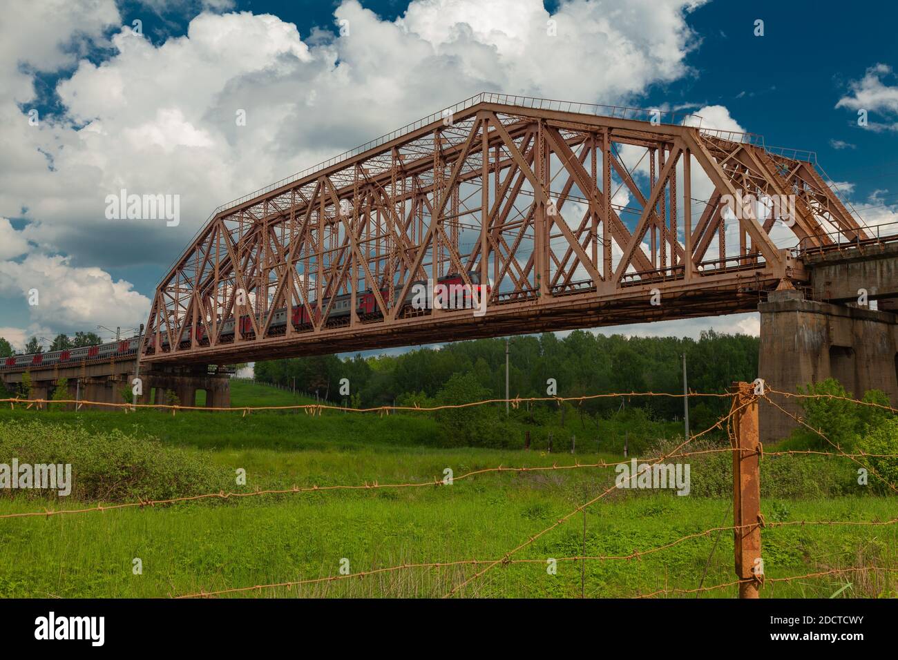 Suburban train rides on a high old iron bridge with concrete piers ...