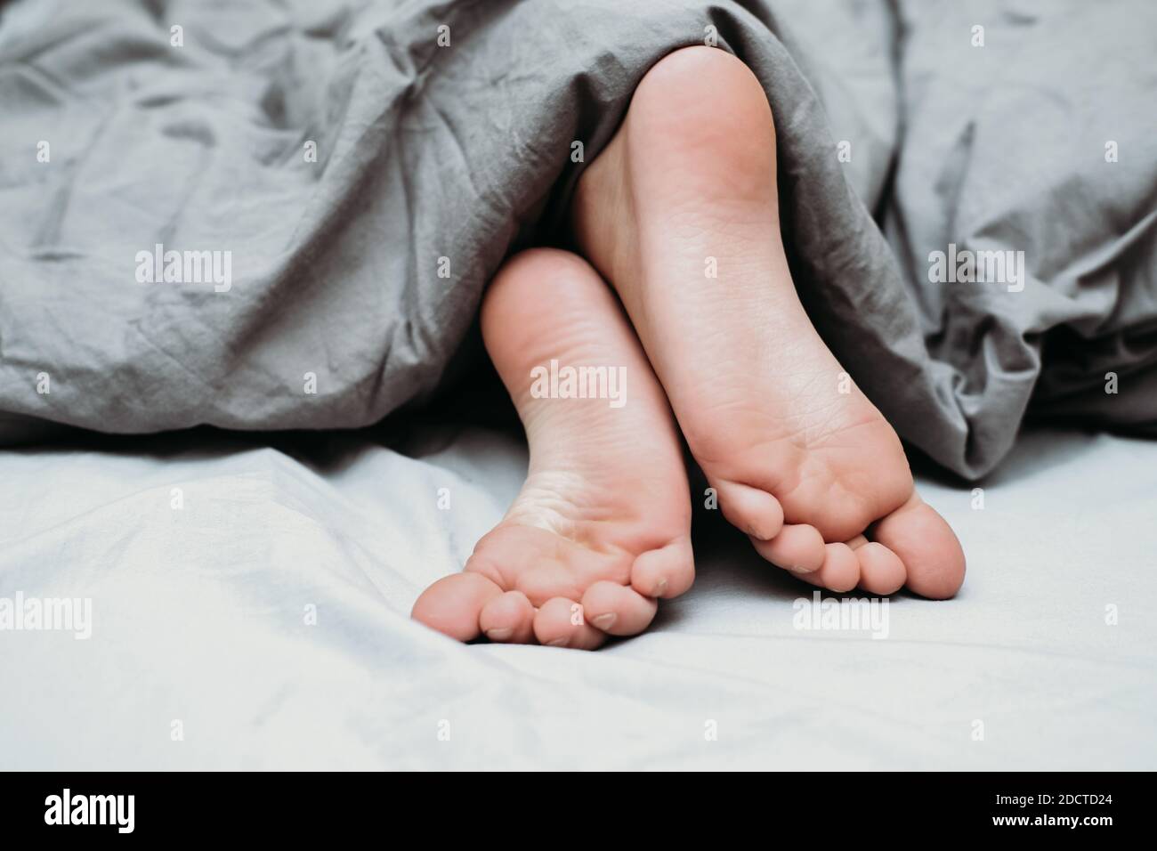 girl's feet covered with bed sheet. crop view of a girl in the bed ...