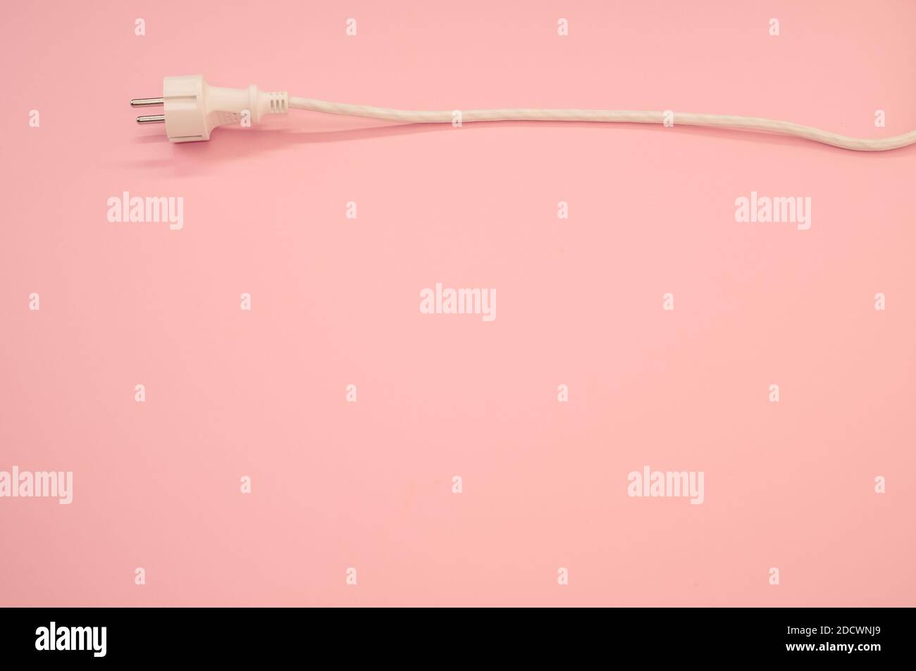 A high angle shot of an electrical wire and plug on a pink surface ...