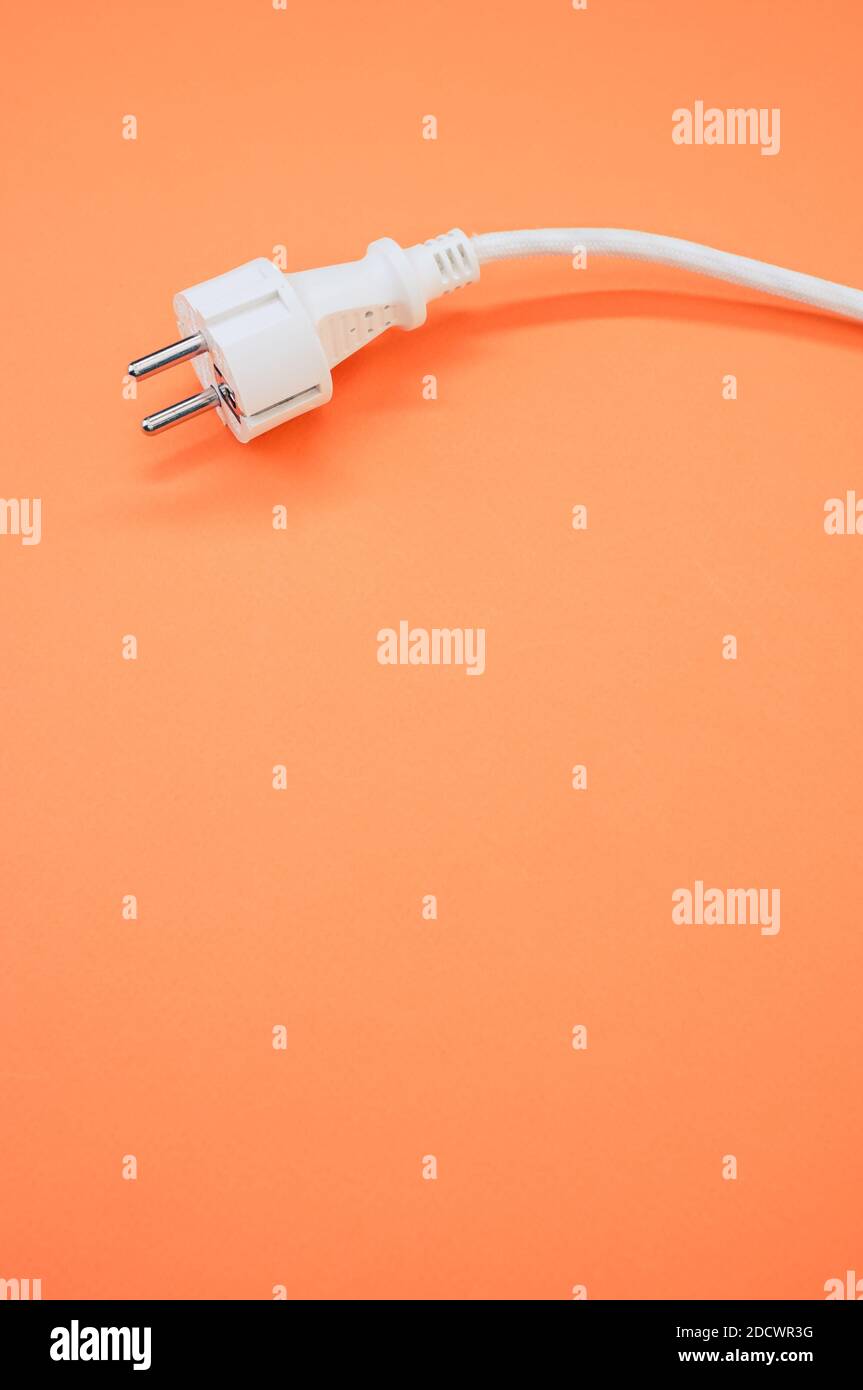 A vertical shot of an electrical wire and plug on an orange surface ...