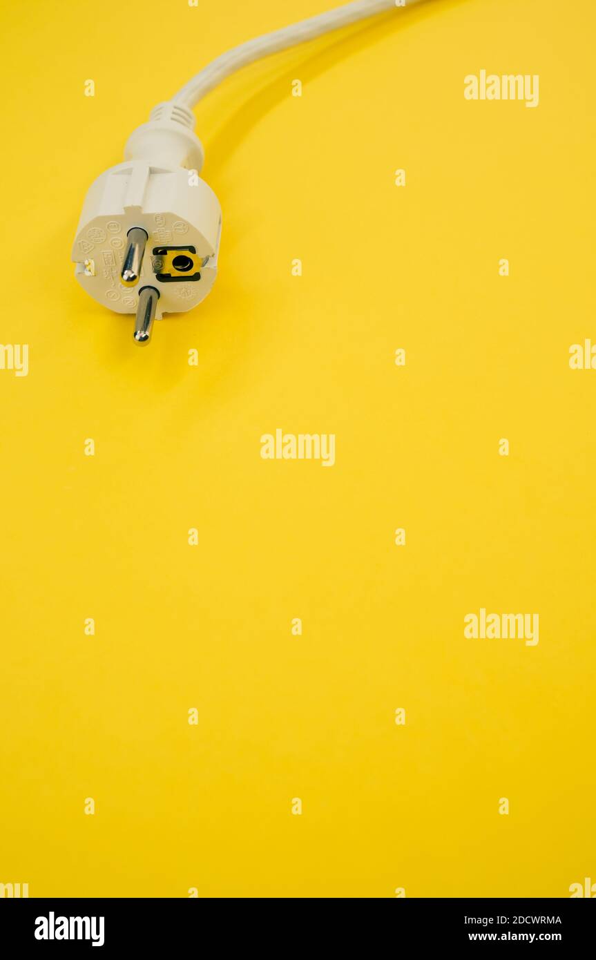 A vertical shot of an electrical wire and plug on a yellow surface ...