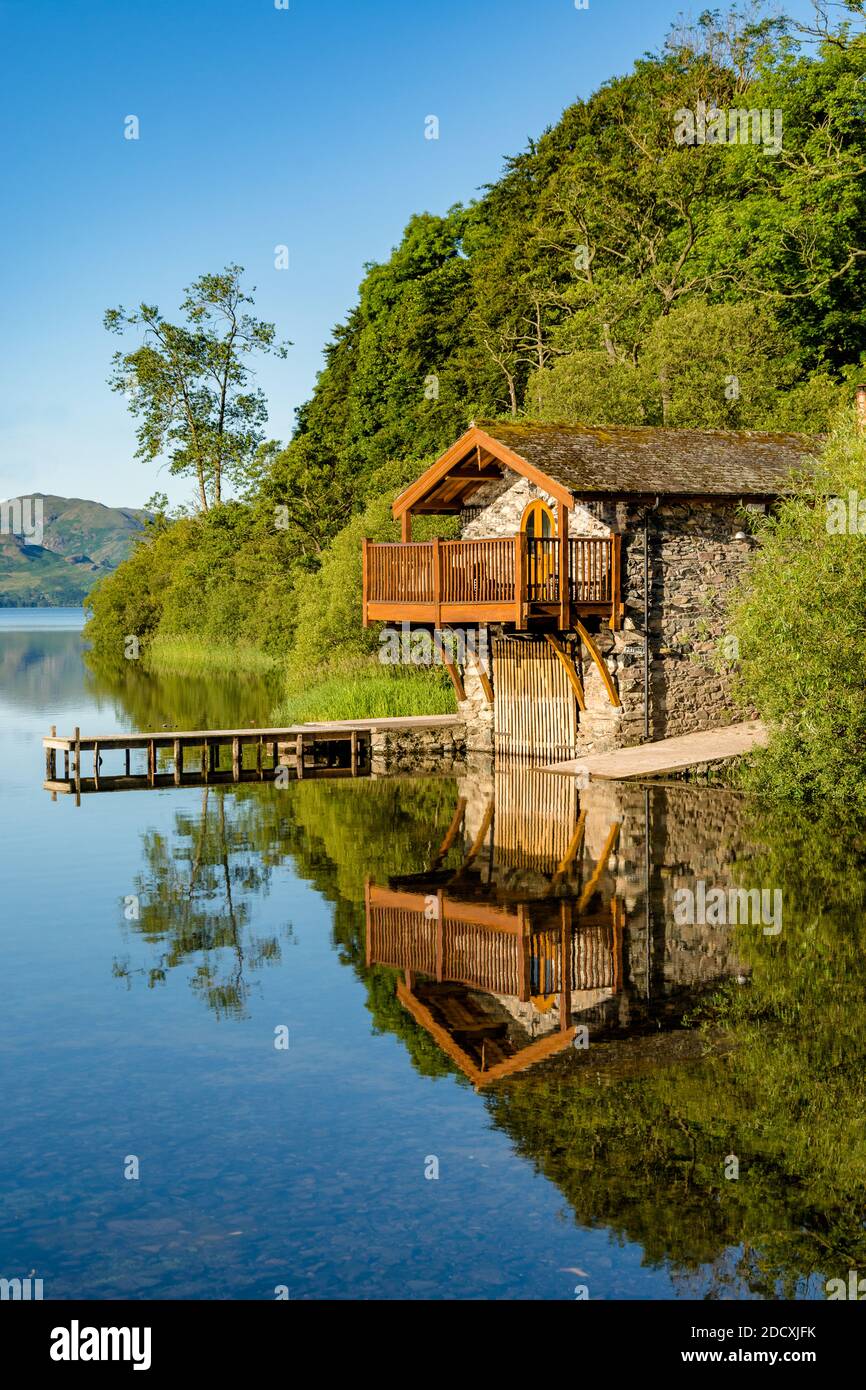 Boathouse and jetty with clear calm reflections in lake. Ullswater ...