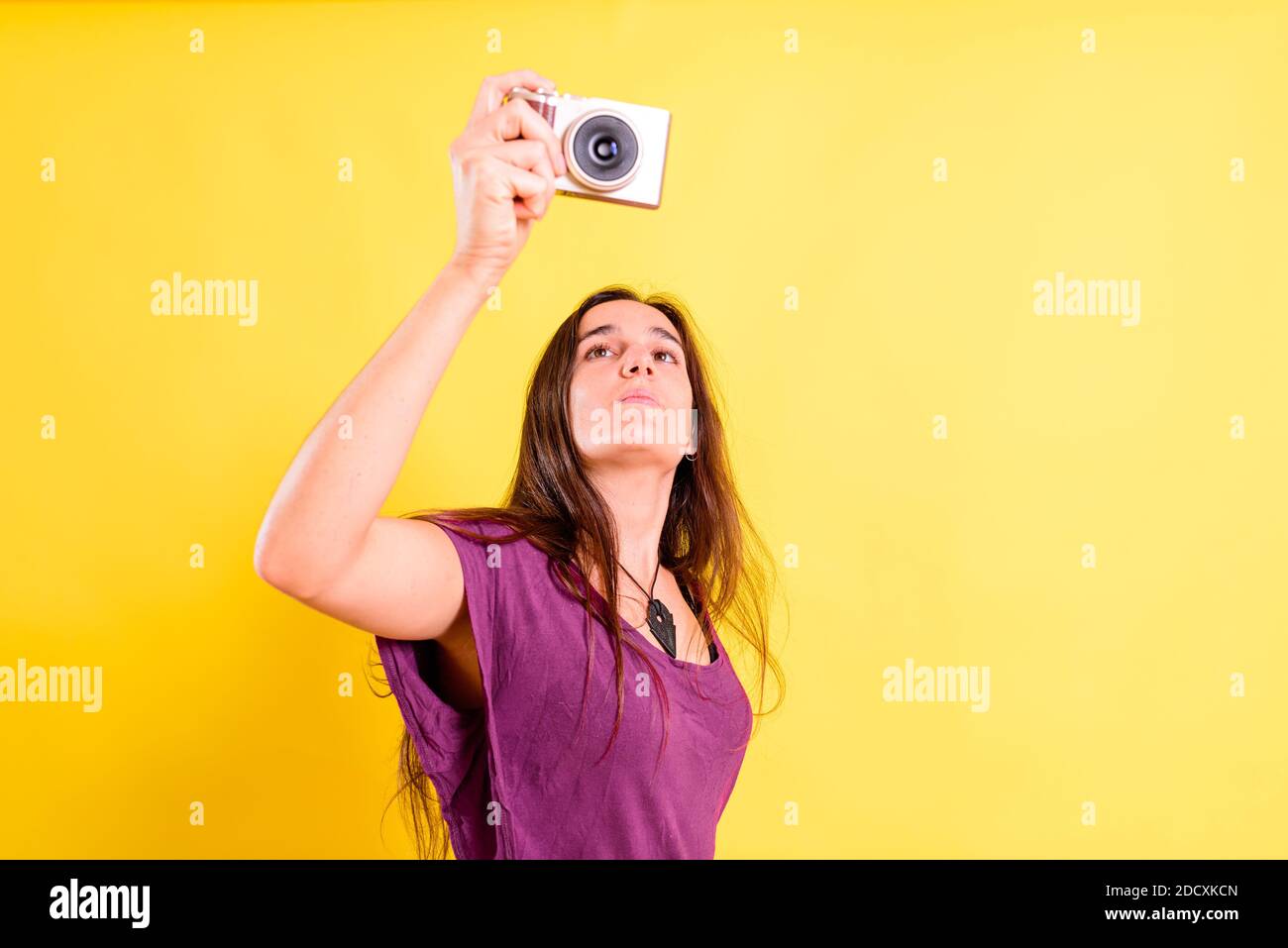 Pretty young girl takes photos with an evil camera, isolated on yellow ...