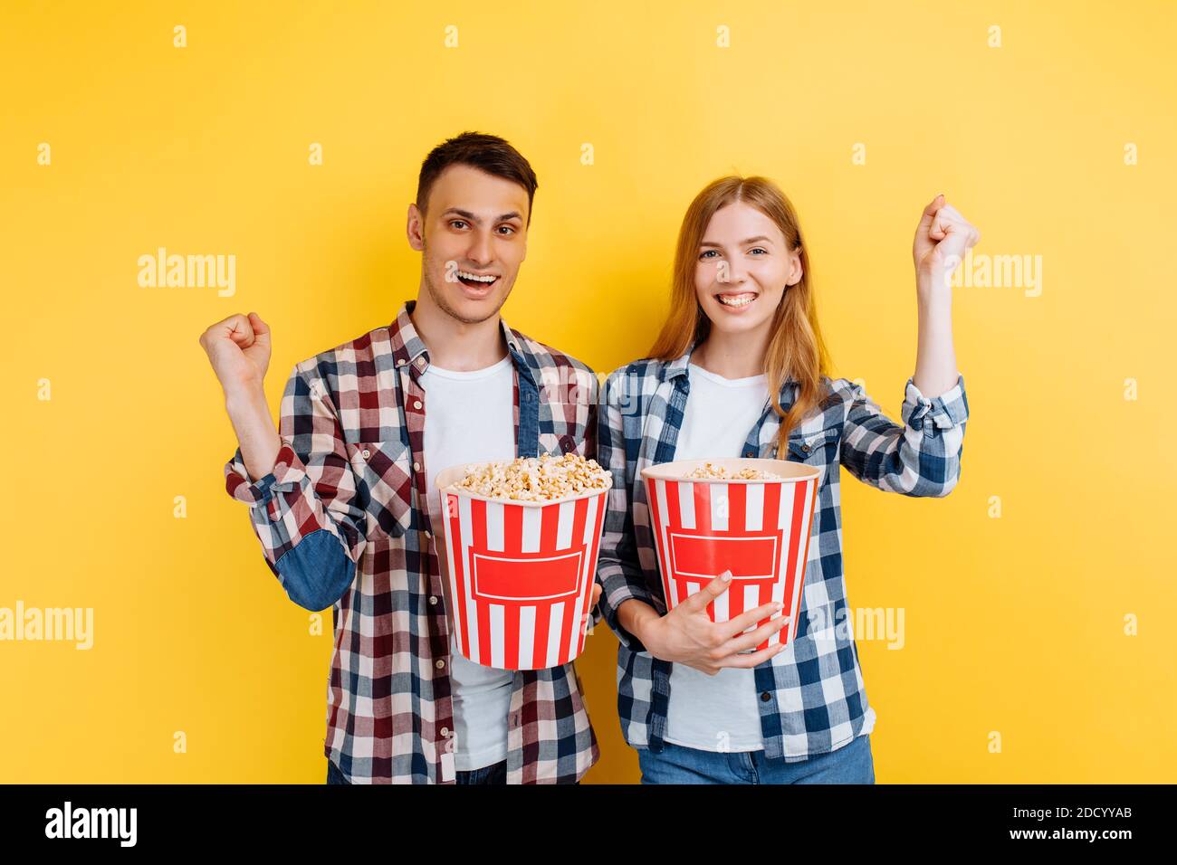 excited young couple watching movie with popcorn on yellow background ...