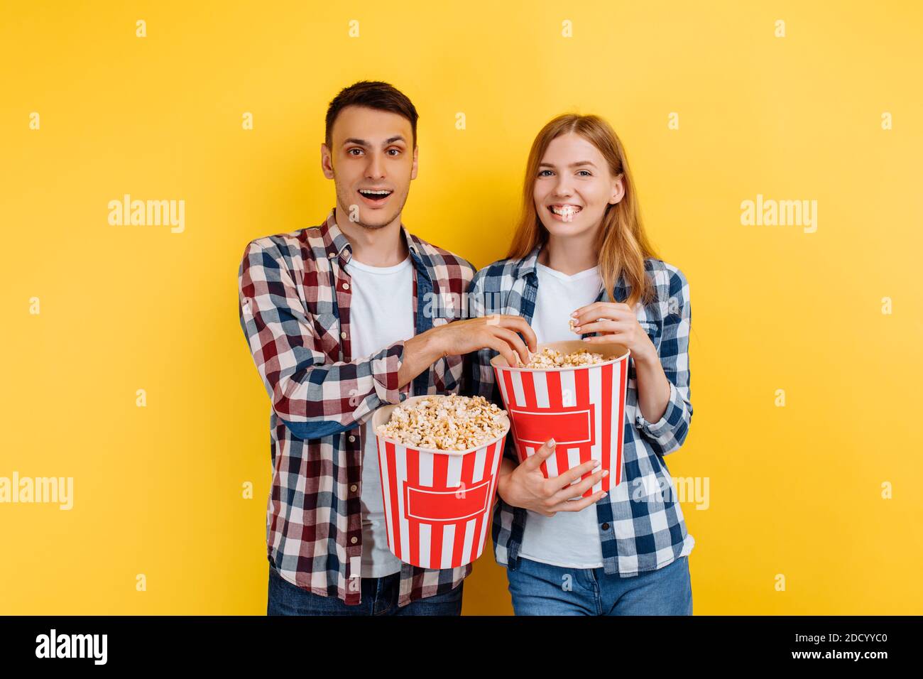 Shocked couple, man and woman with popcorn on yellow background Stock ...
