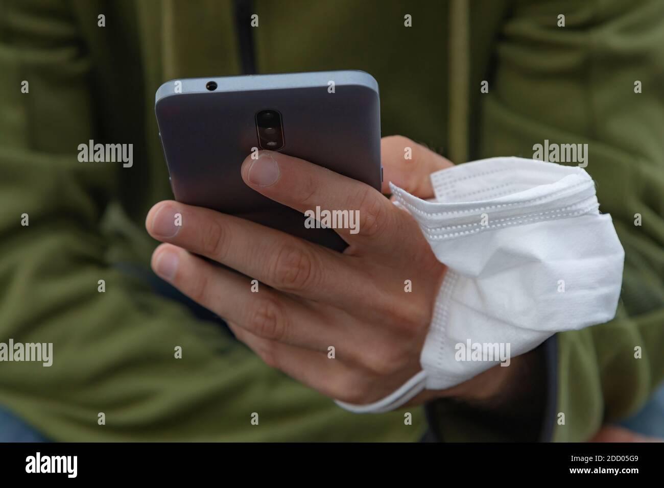 A young man, grabbing a protective face mask, holds a smart mobile ...