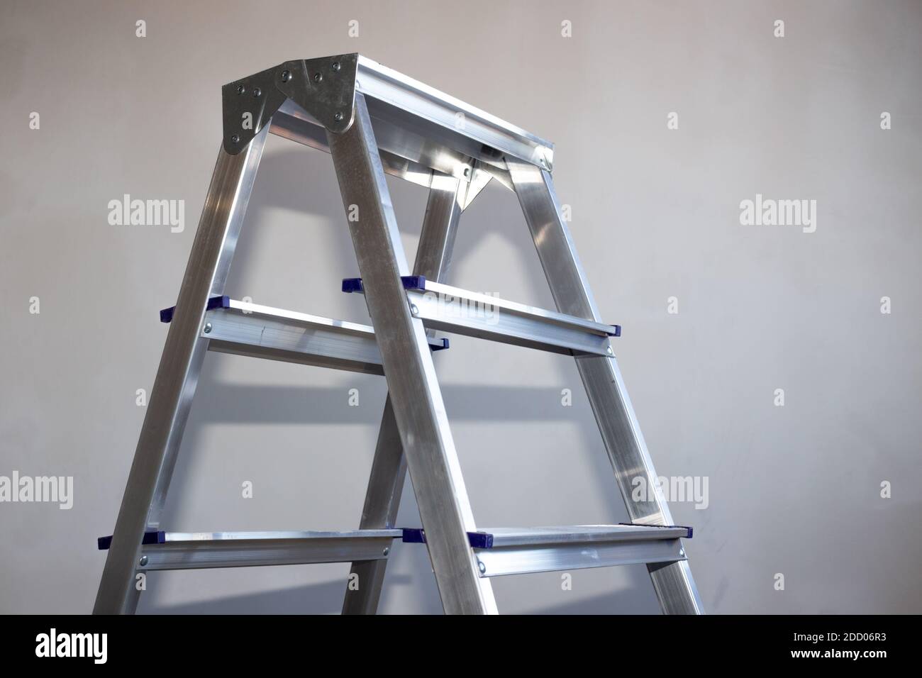 an iron step-ladder stands in a room with gray plastered walls, a copy ...