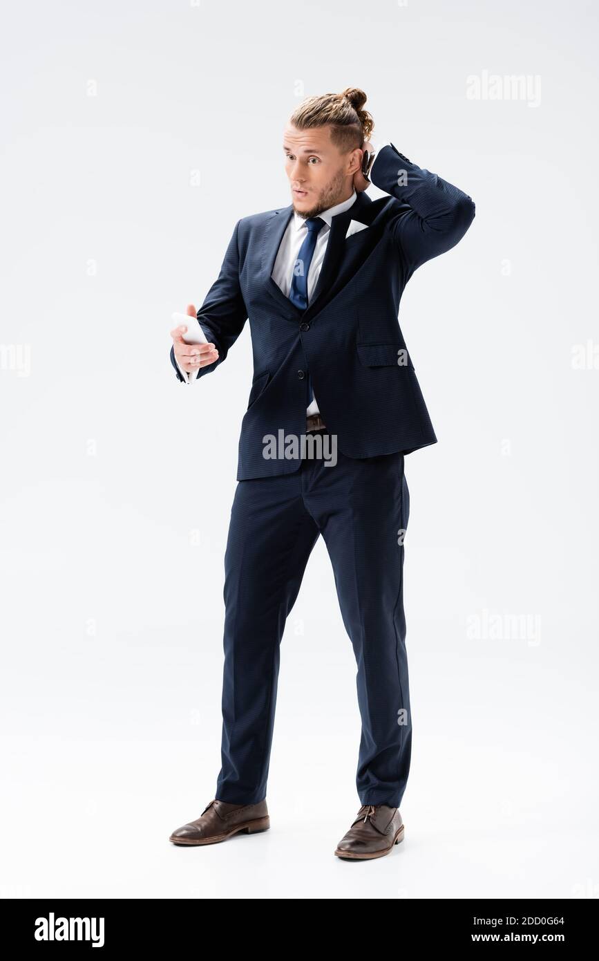 confused young businessman in suit with smartphone isolated on white ...
