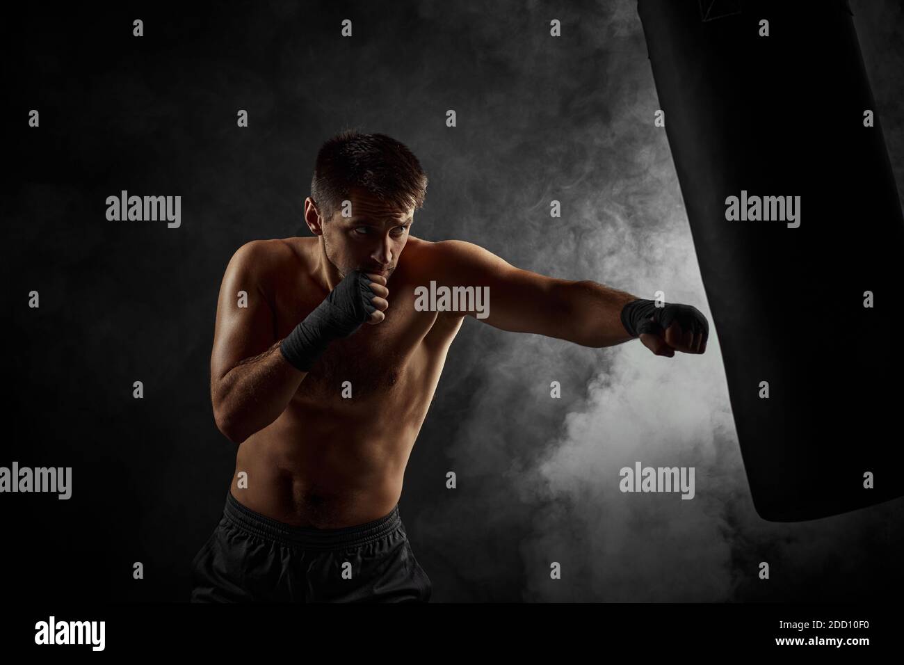 Aggressive shirtless boxer training defense and attacks in boxing bag ...