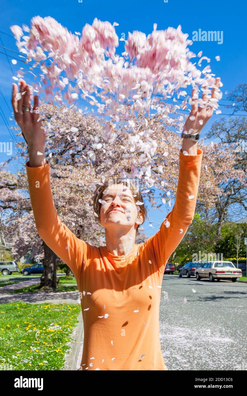 Happy woman throwing tree blossom petals in the air during Spring in ...