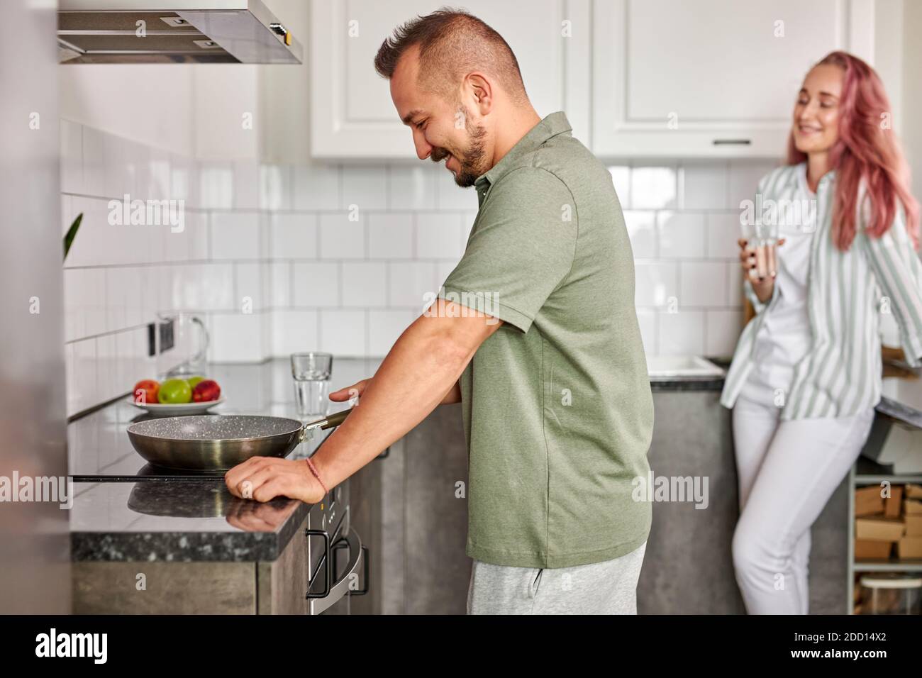 side view on male cooking in the kitchen while his wife stand in the ...