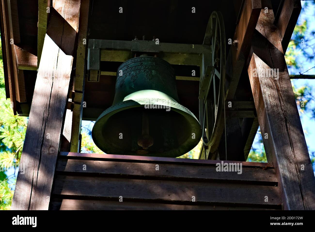 Bronze church bell with green patina, mounted in a brown wooden tower ...