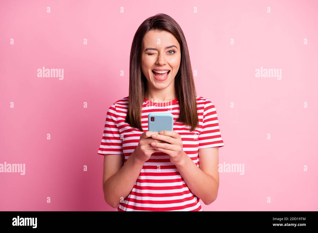 Photo of cute funky young lady hold smartphone wink wear casual outfit isolated over pastel pink ...
