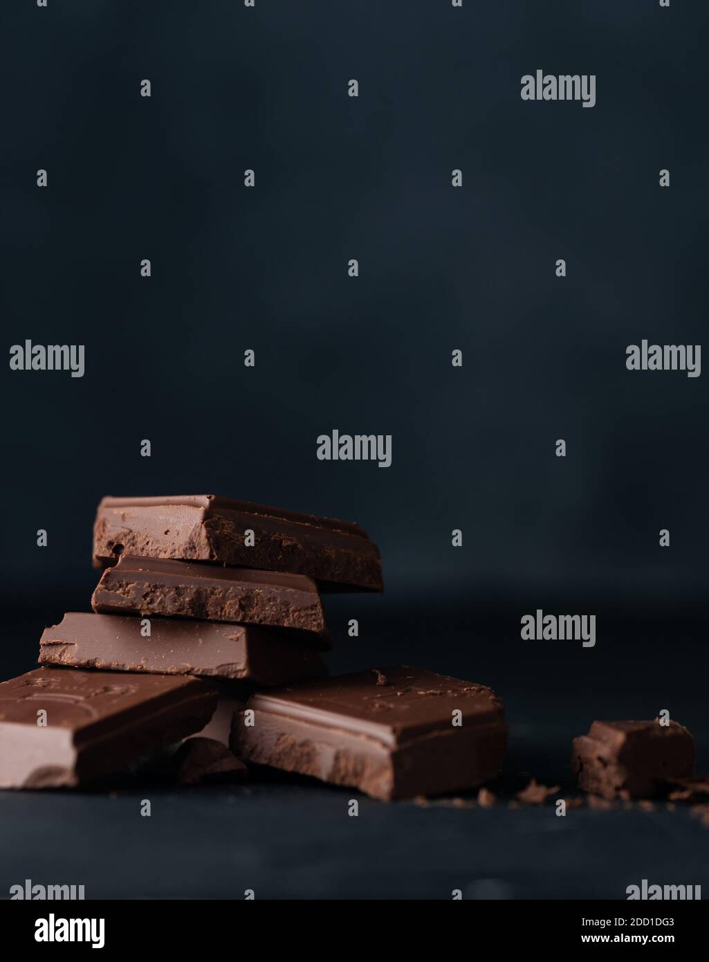 A vertical shot of chocolate bars broken into pieces in a dark room ...