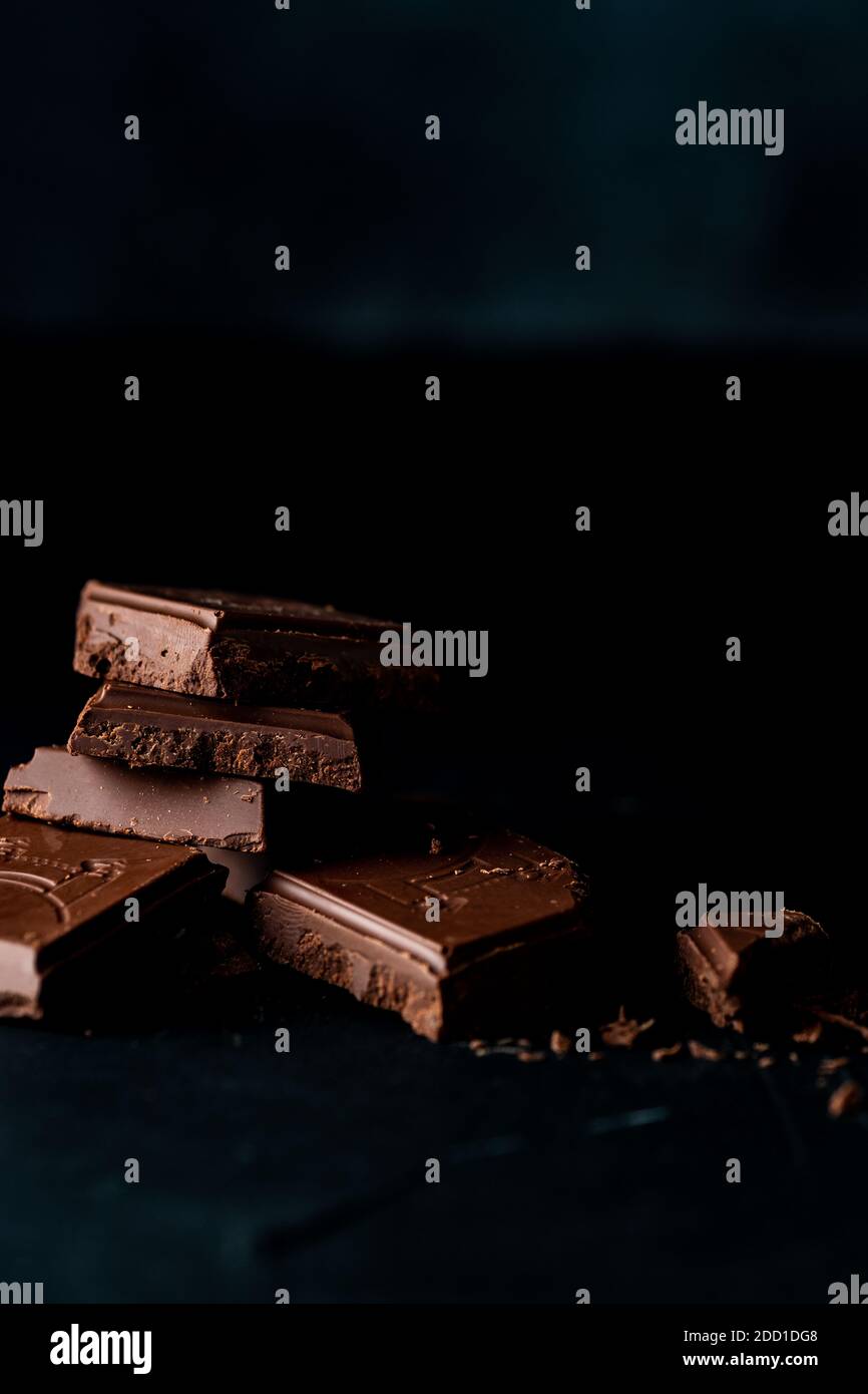 A vertical shot of chocolate bars broken into pieces in a dark room ...
