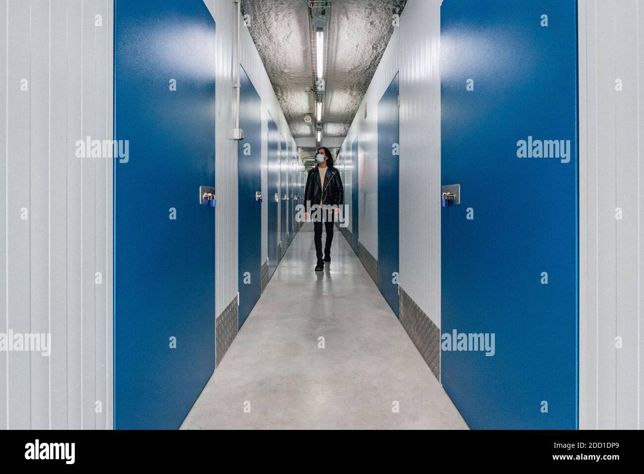 A Hispanic man in a leather jacket walking in a hallway with blue doors ...