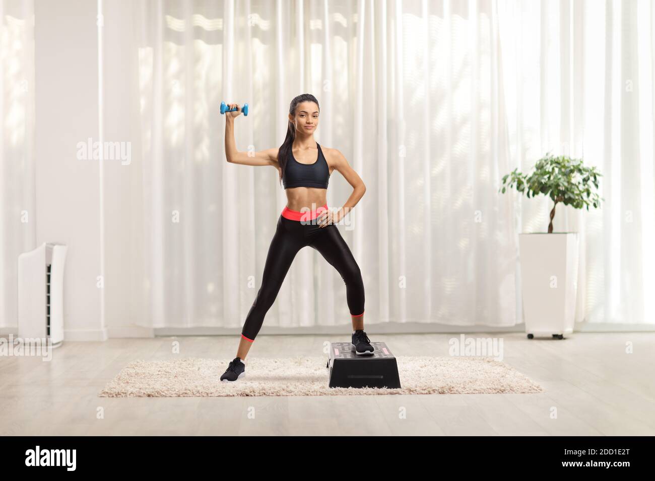 Full length portrait of a young woman exercising step aerobic with a ...