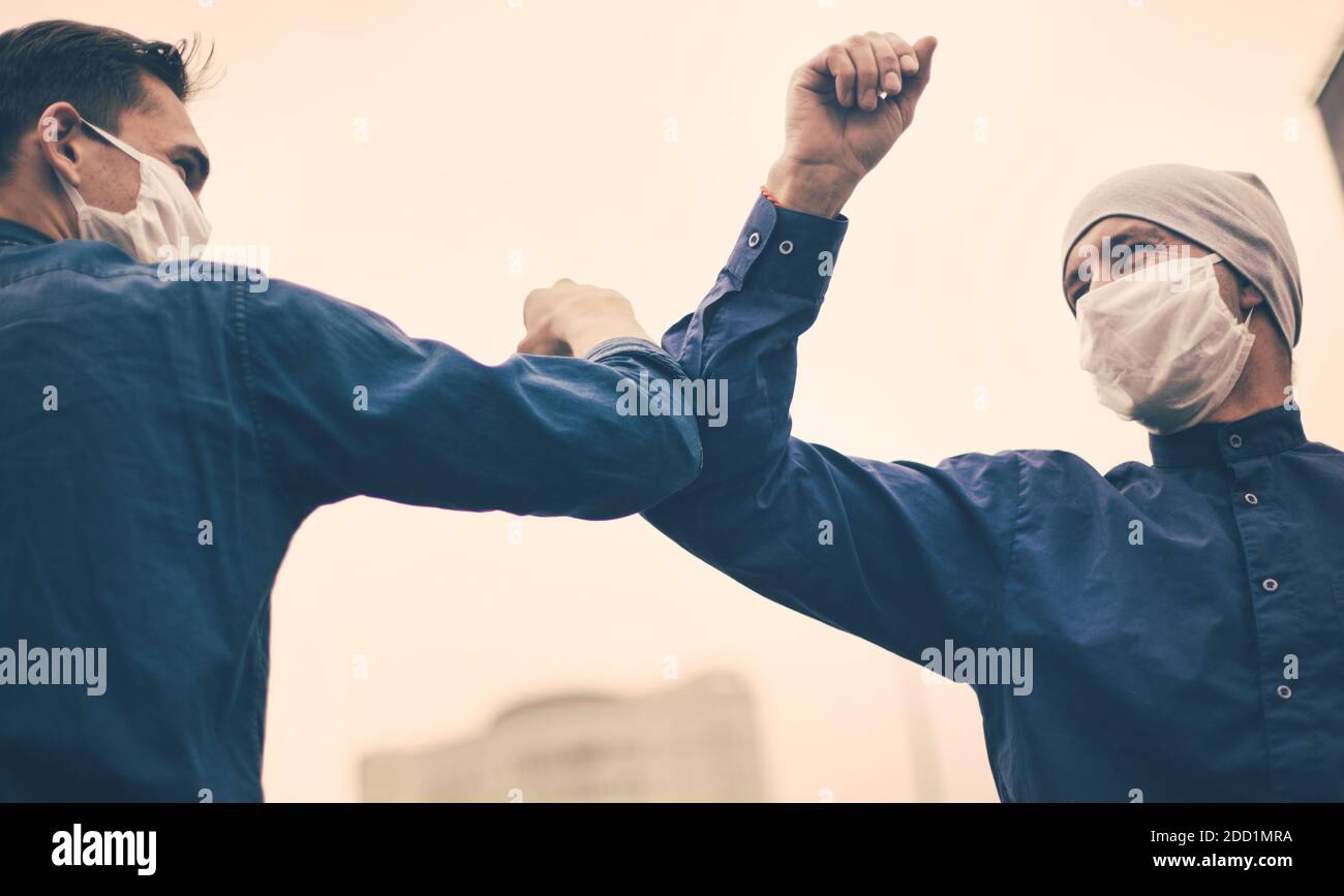 two friends greeting each other with their elbows on a city street ...