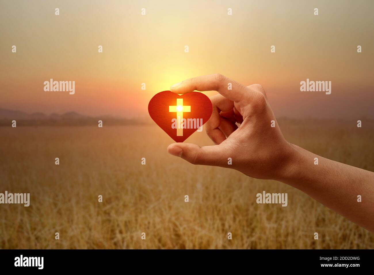 Human hand holding a red heart with a Christian cross with a sunrise ...