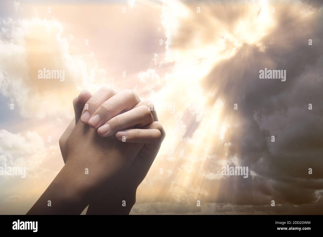 Human hands raised while praying to god with a dramatic sky background ...