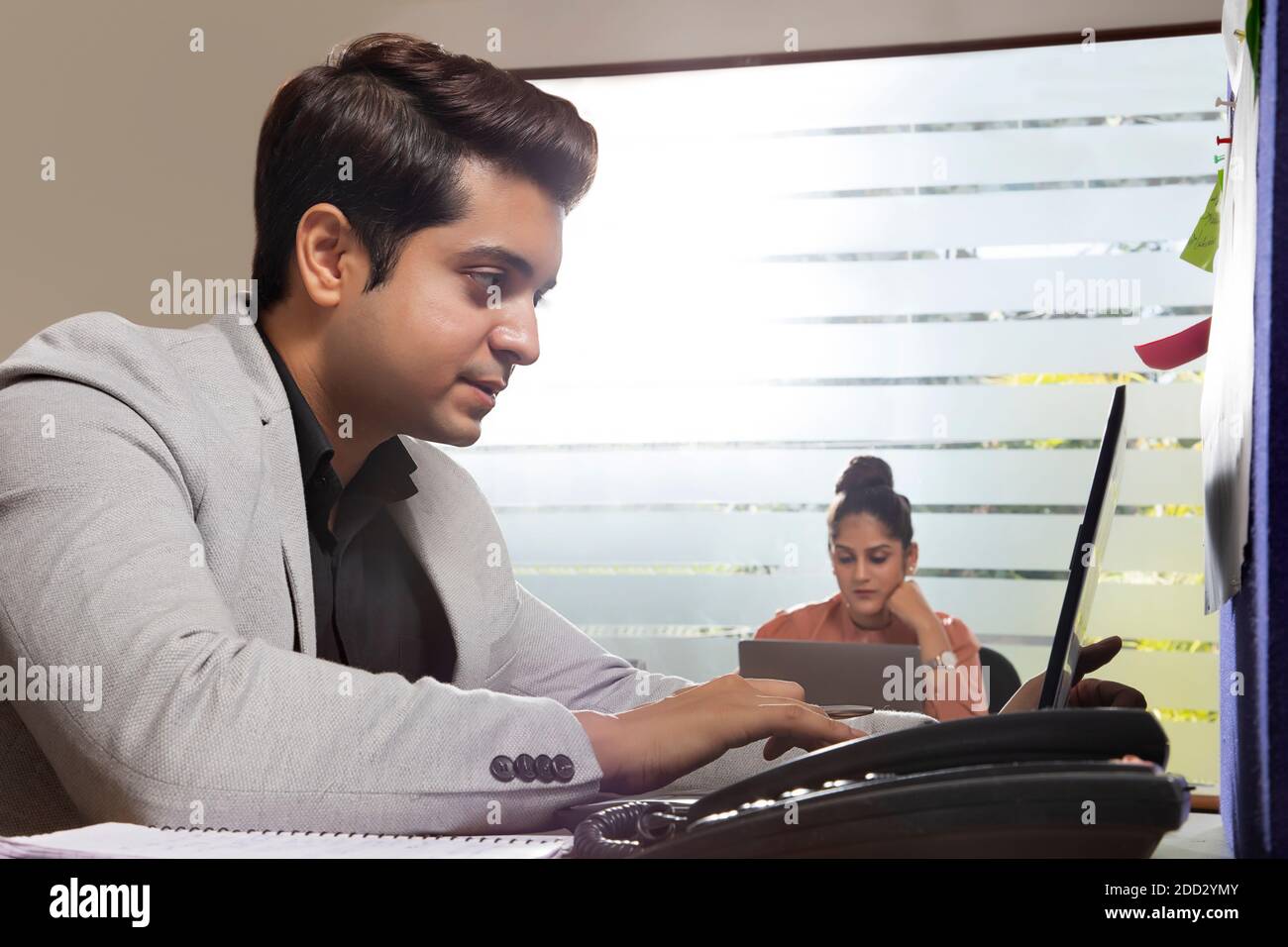 AN OFFICE EXECUTIVE WORKING IN HIS CUBICLE WITH A COLLEAGUE VISIBLE ...