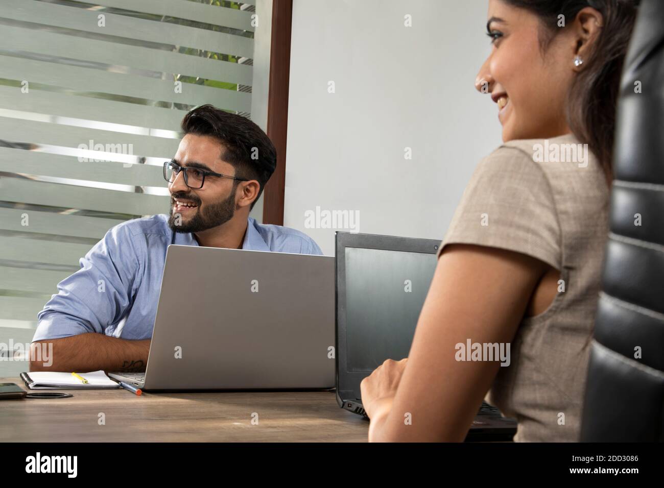 A YOUNG MAN AND WOMAN HAPPILY LOOKING AT COLLEAGUE WHILE WORKING Stock ...
