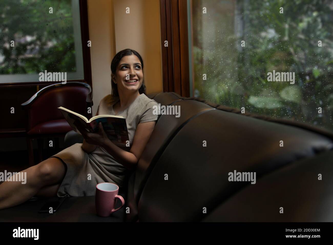 A YOUNG WOMAN READING A BOOK AND LOOKING OUTSIDE WHILE ITS RAINING ...