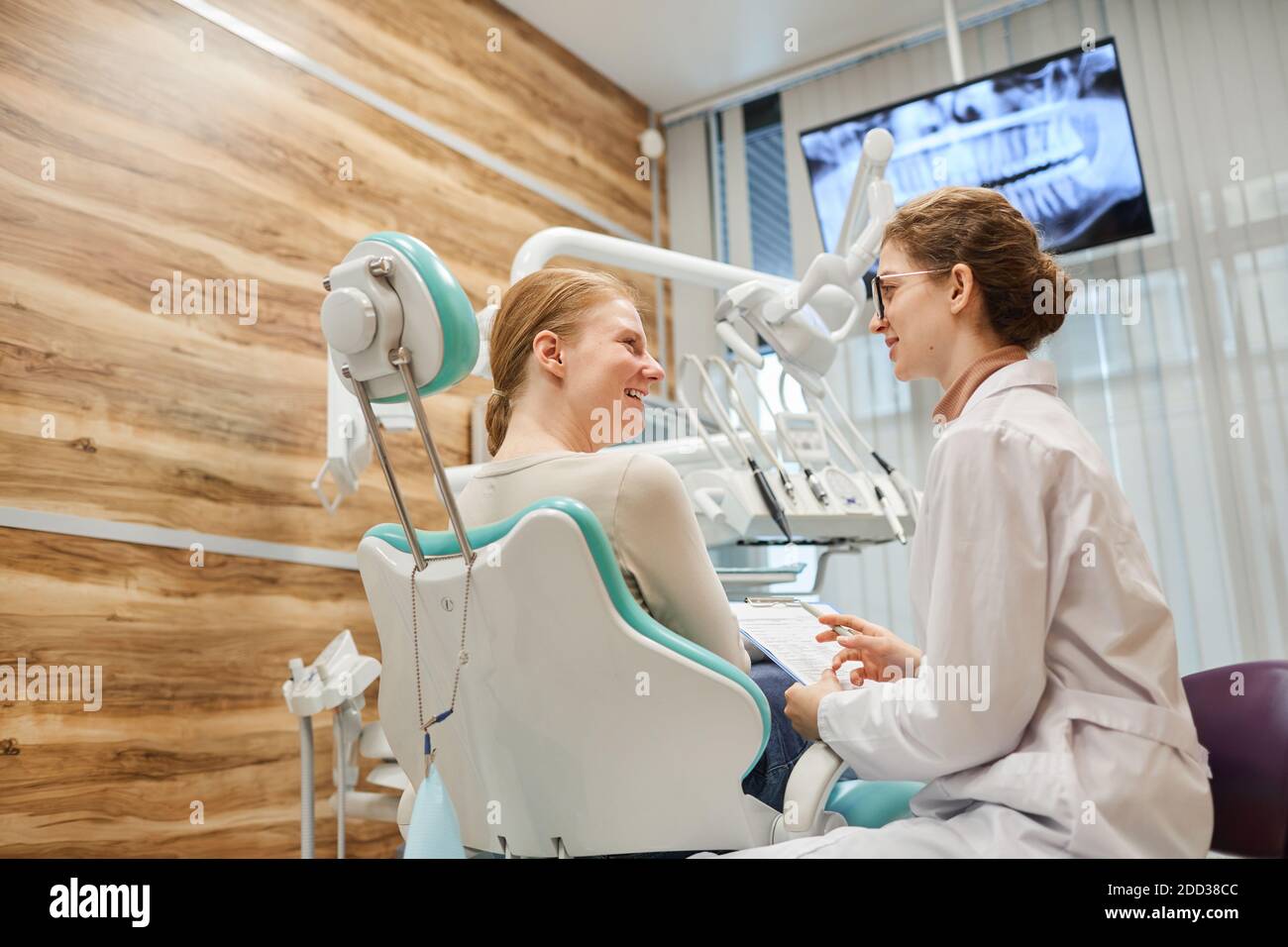 Young woman sitting on dental chair and consulting with dentist during ...