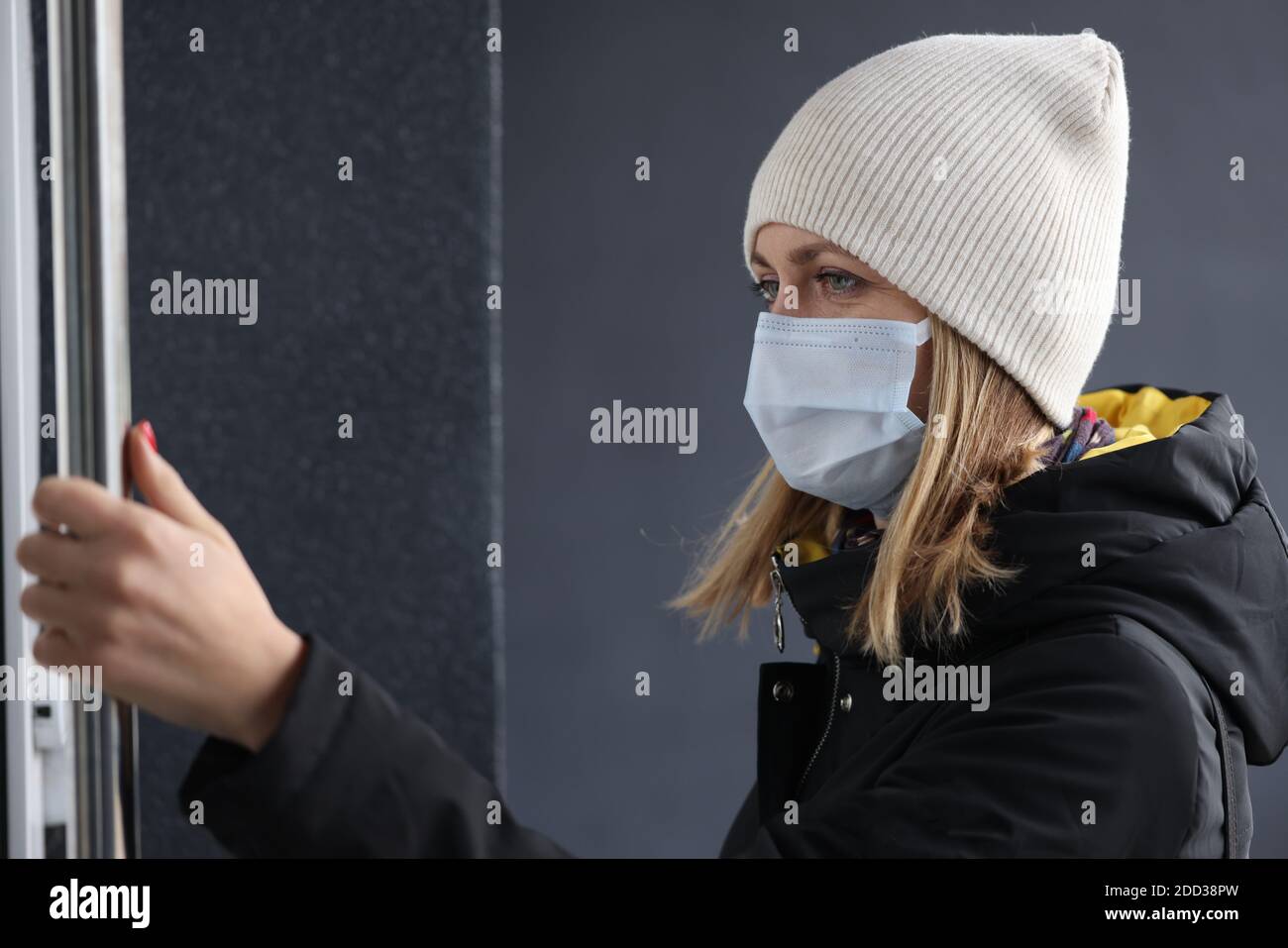 Woman in warm clothing and protective face mask holding on to door ...