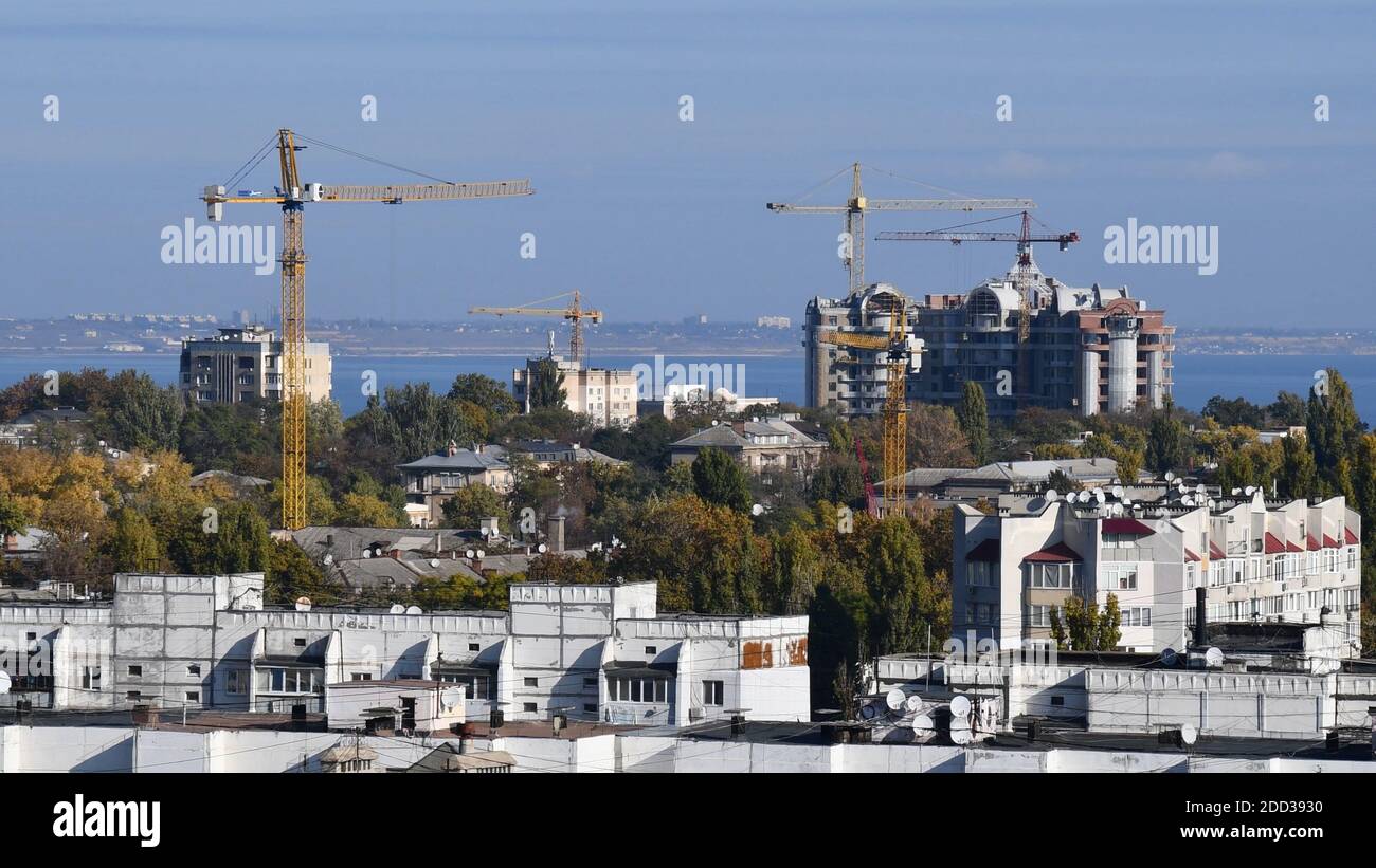 Construction cranes jibs over rooftops between autumn tree foliage ...