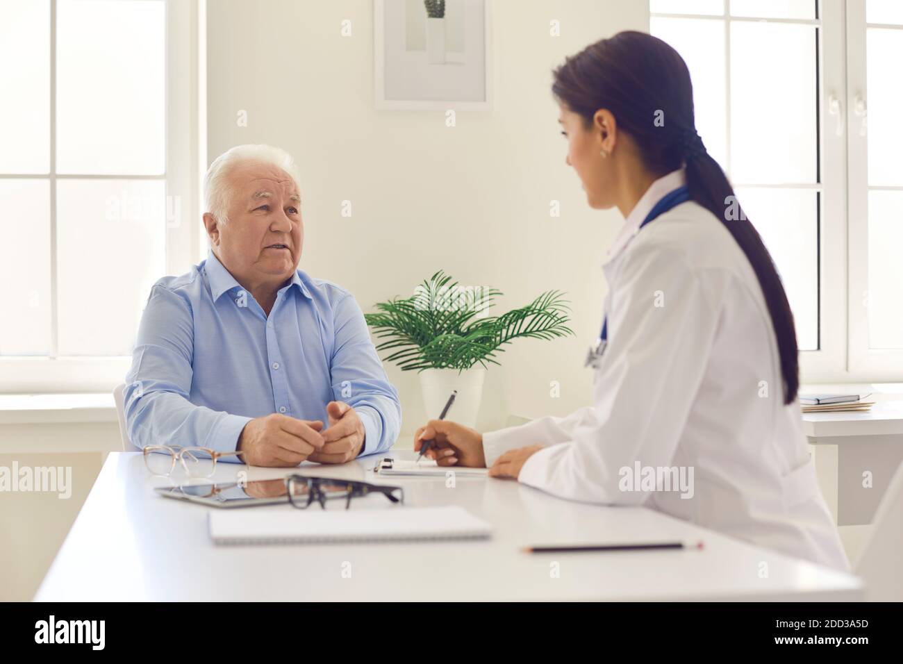 Senior patient consulting young doctor sitting at desk in modern ...