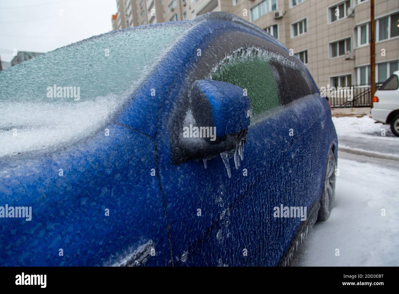 The blue car is covered with a thick crust of ice, freezing rain, in ...