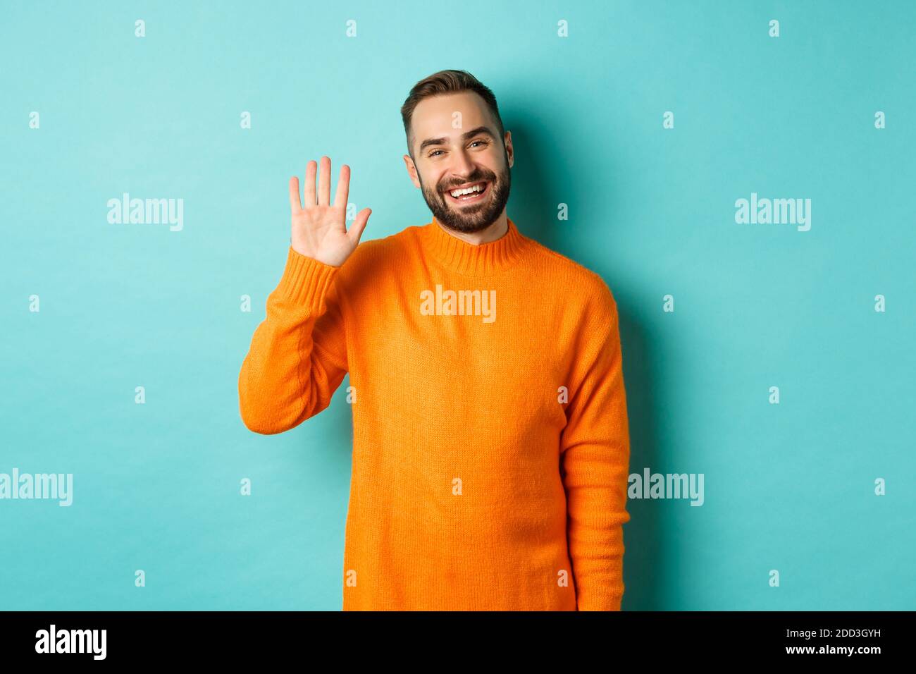 Photo of friendly young man saying hello, smiling and waiving hand ...