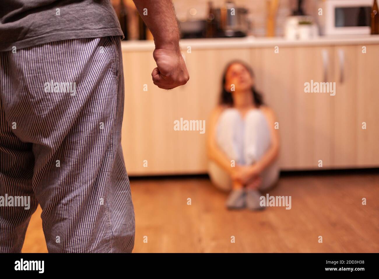 Brutal man clenching fist sitting in front of abused woman. Traumatised ...
