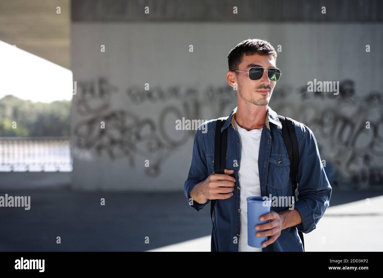 Front view of young attractive man with backpack standing outdoors in ...
