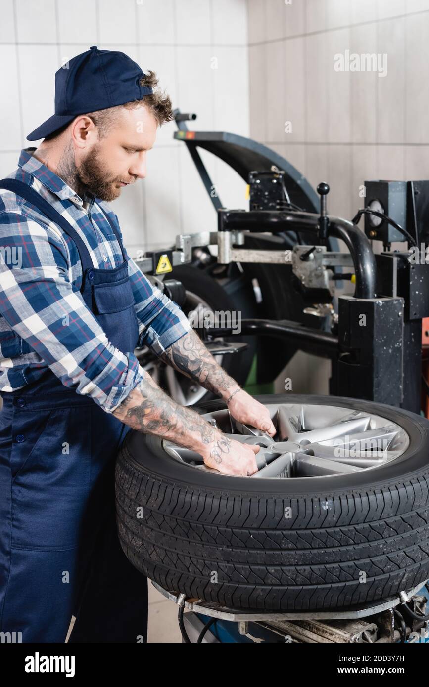 tattooed technician putting wheel on tire changing machine in workshop ...
