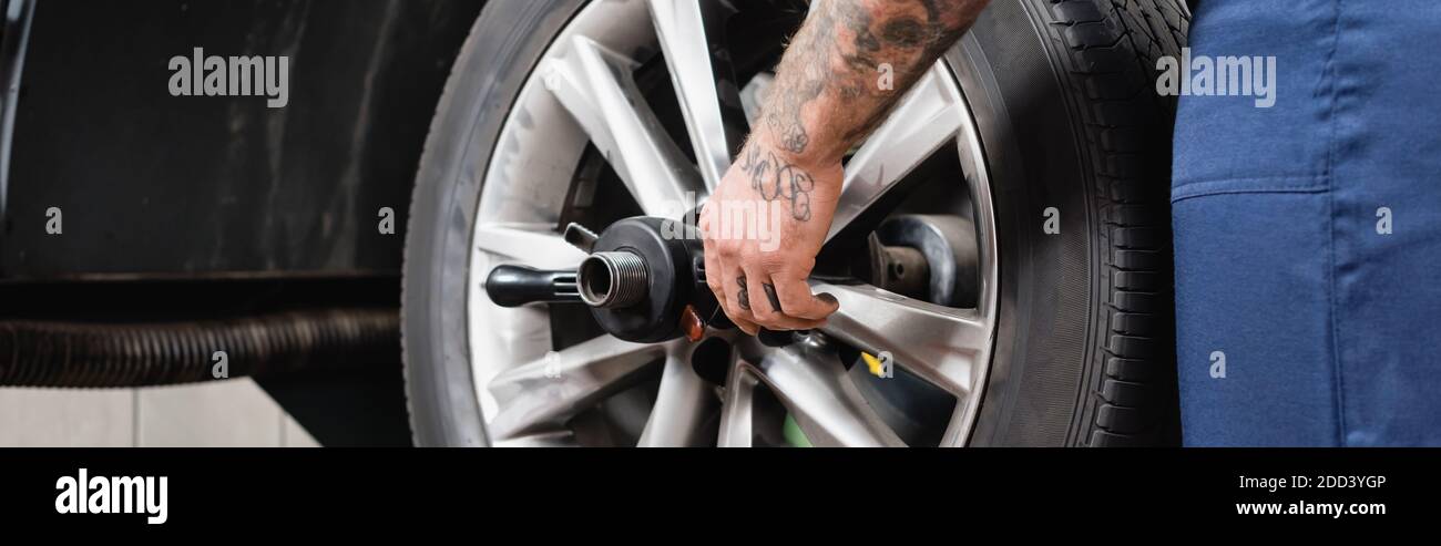 partial view of tattooed mechanic adjusting car wheel, banner Stock ...