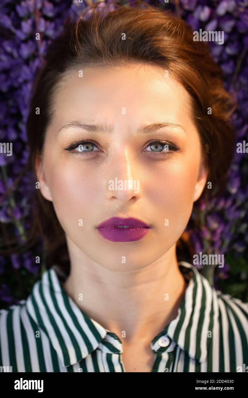 beautiful girl with lilac lips, lying on purple flowers backdrop in ...