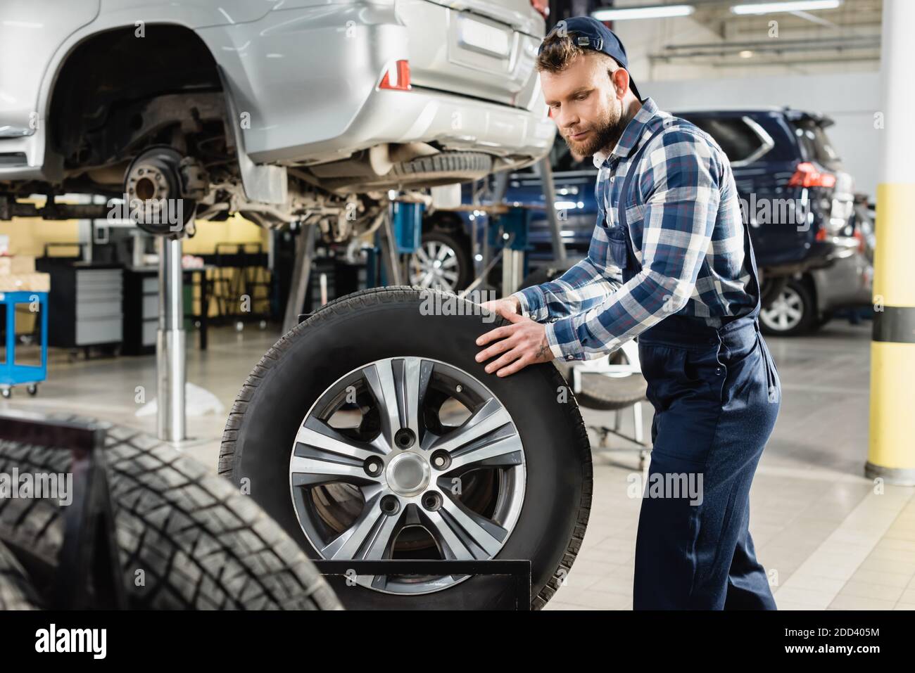 mechanic in overalls moving wheel near vehicle raised on car lift Stock ...