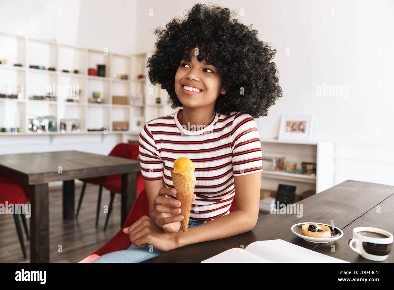 Smiling african american student girl eating ice cream while drinking ...