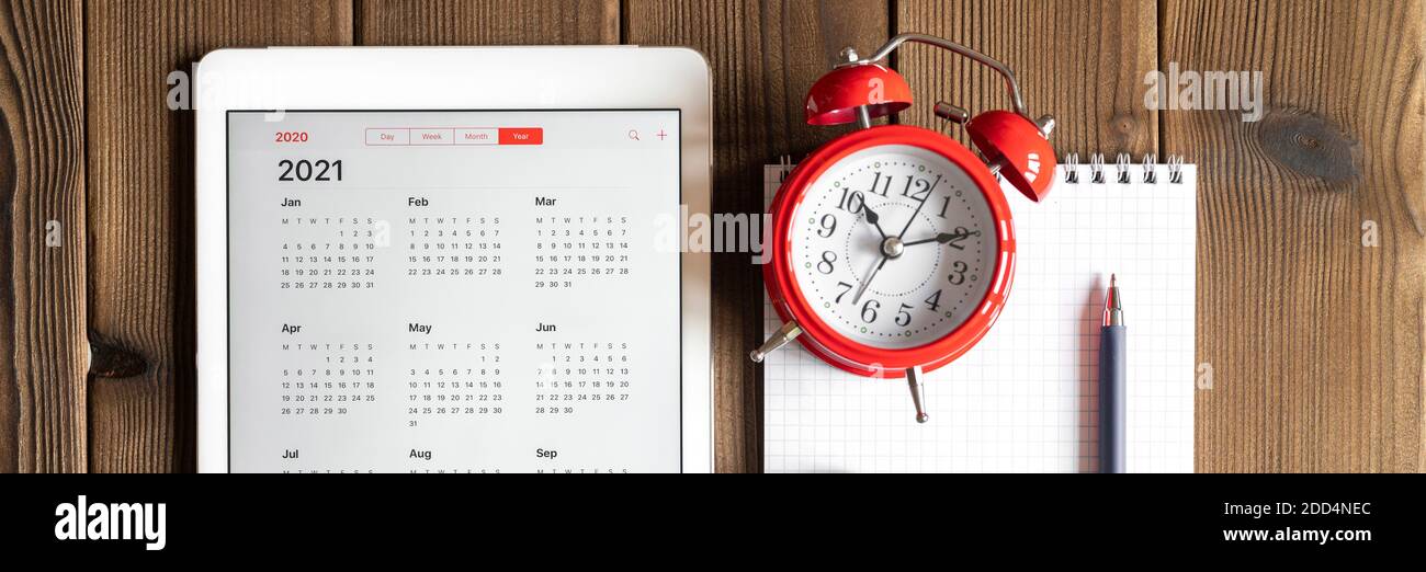 a tablet with an open calendar for 2021 year, a red alarm clock ...