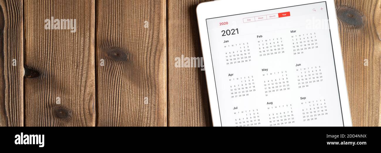 a tablet with an open calendar for 2021 year on a wooden boards table ...