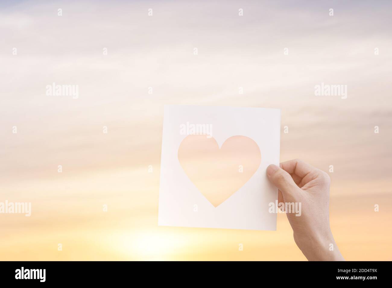 Silhouette of hand is raising paper with shape heart at sunset ...