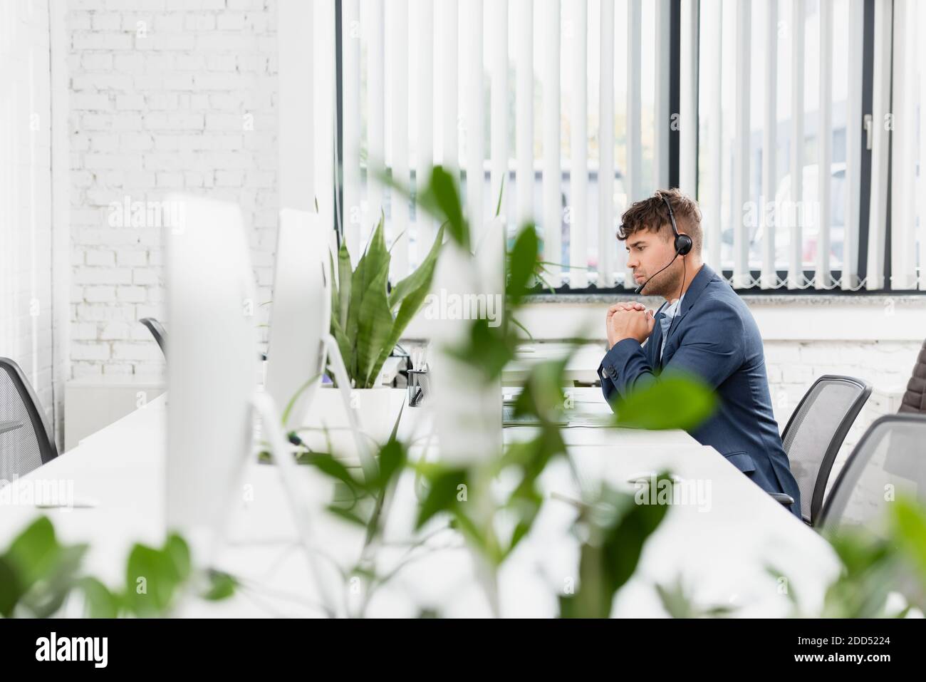 Serious operator in headset sitting at workplace in office with blurred ...