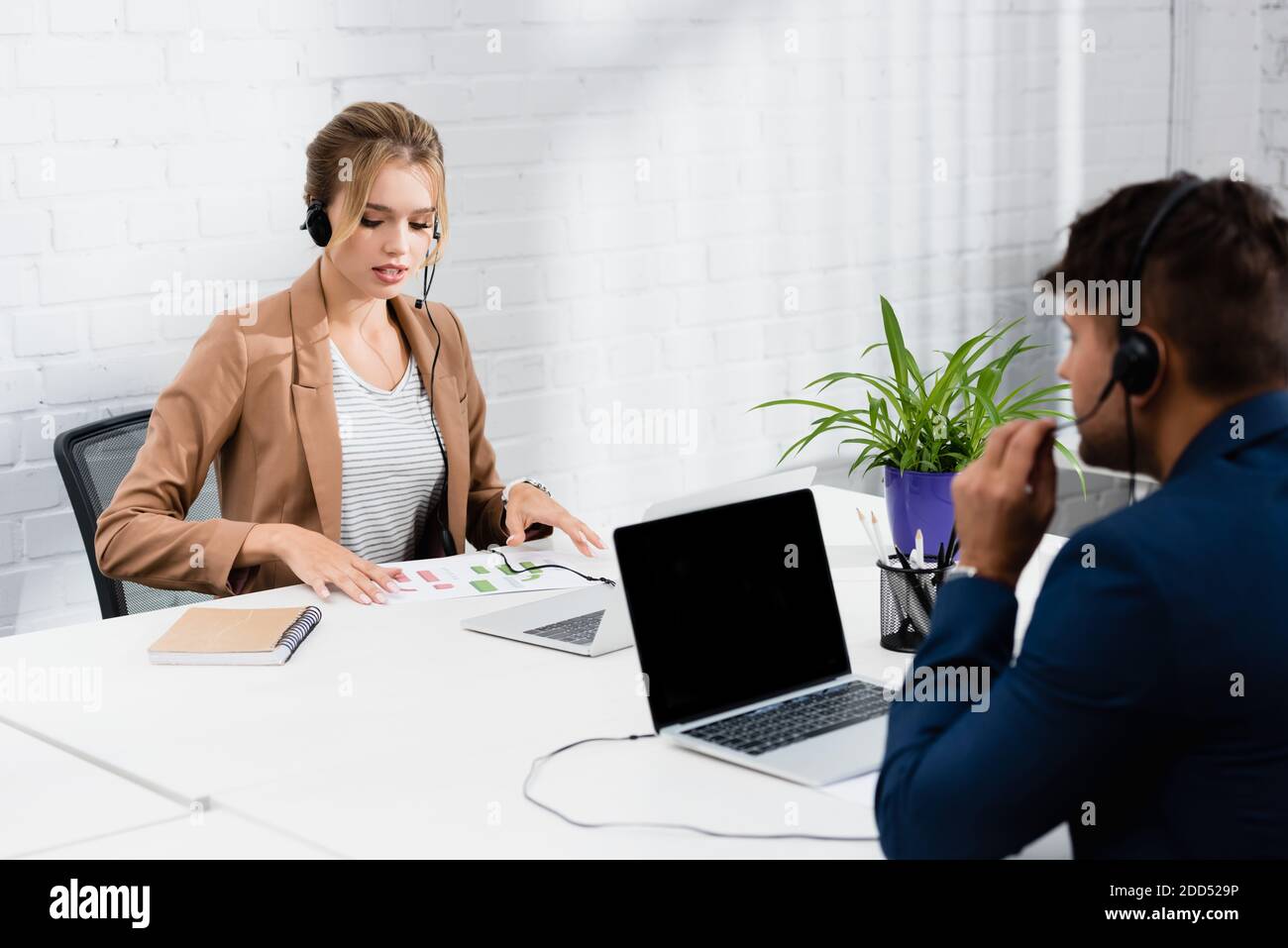 Female operator in headset talking, while looking at charts on sheet of ...