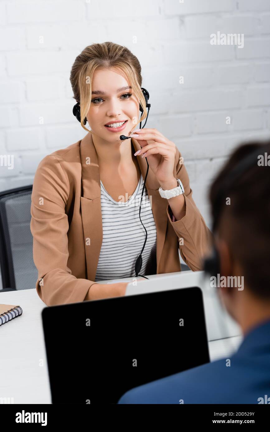 Positive female operator in headset looking at colleague, while sitting ...