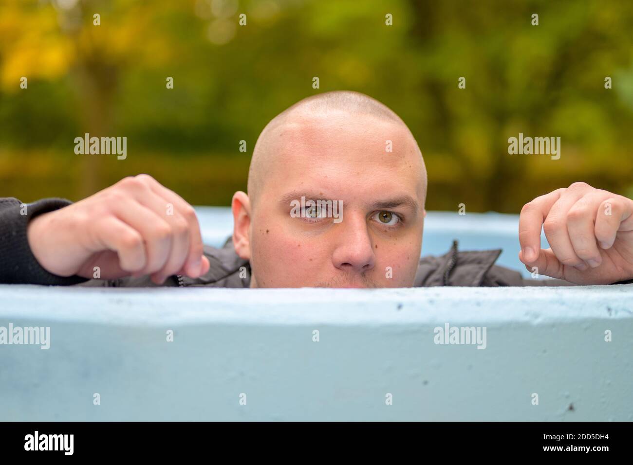Serious young man looking at camera over rim of a tank or outdoor pool ...